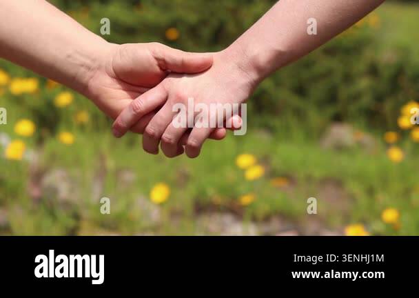 Two people holding hands on a background of nature with flowers. Close ...