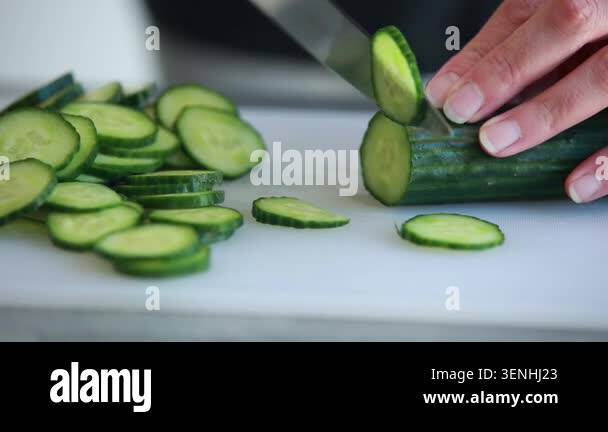 Close-up of a woman's hands slicing a fresh green cucumber with a chef ...