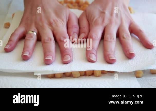 Close-up of a woman's hands using kitchen paper to dry cooked chickpeas ...