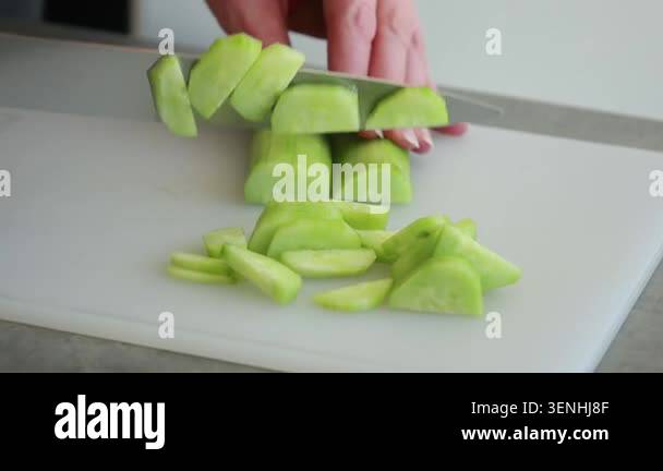 Close-up of a woman's hands slicing a fresh green cucumber with a chef ...