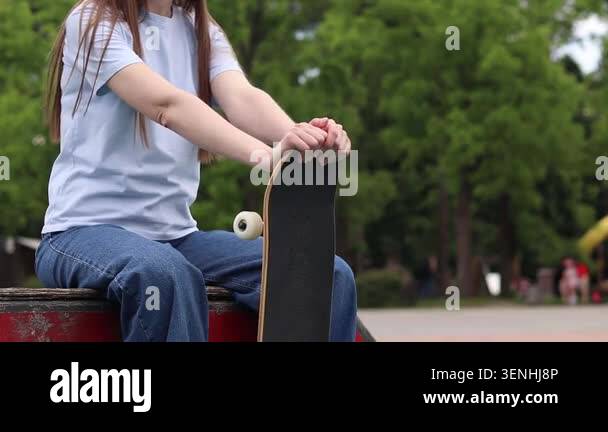 Girl sitting on a ramp and holding a skateboard. Close-up of a teenage ...