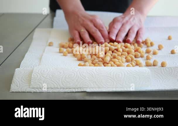 Close-up of a woman's hands using kitchen paper to dry cooked chickpeas ...