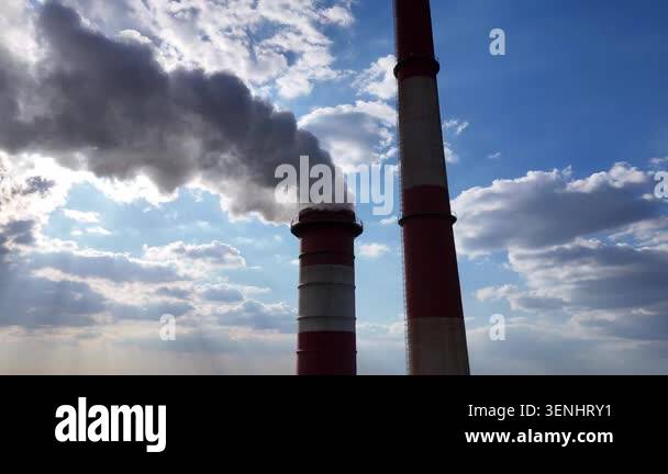 Industrial smokestacks emit white smoke against a bright sky, with ...