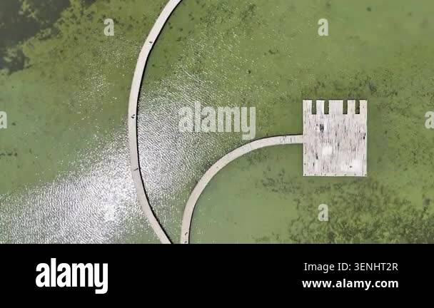 Aerial view of a winding wooden bridge over a serene pond, leading to a ...