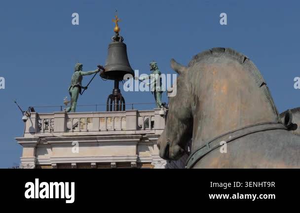 Patinated bronze horse, bell ringers, and golden cross on a historic ...
