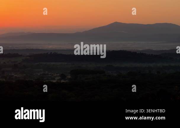 Panoramic morning scene: fog drifts over a quiet valley, with dark ...