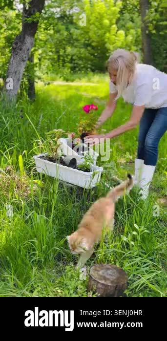 blonde woman in white rubber boots planting flowering plants in a ...