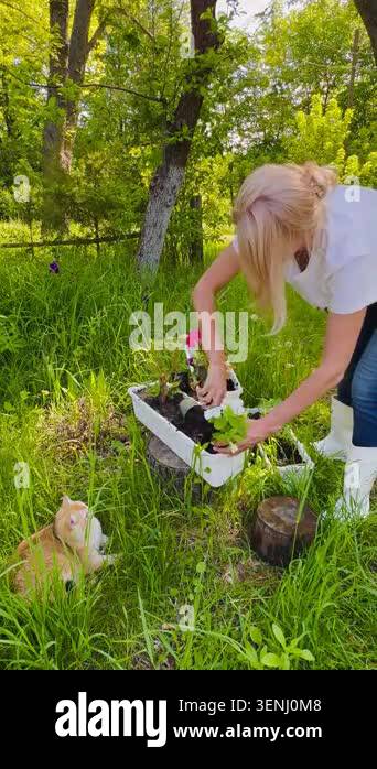 A woman in jeans and white boots is planting pink flowers in a white ...