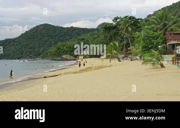 People relax and swim on a golden sand beach flanked by vibrant green ...