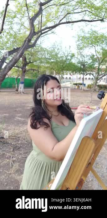 Happy curvy female artist painting on a canvas with a paintbrush ...