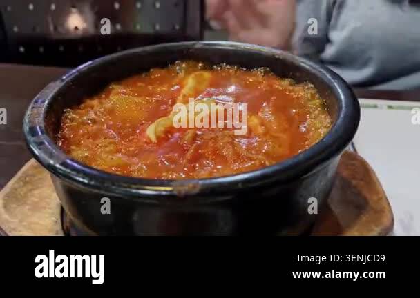 Traditional Korean kimchi jjigae bubbling in hot stone bowl, with ...