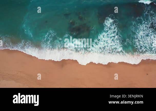 Aerial drone shot of turquoise ocean waves crashing onto sandy beach ...