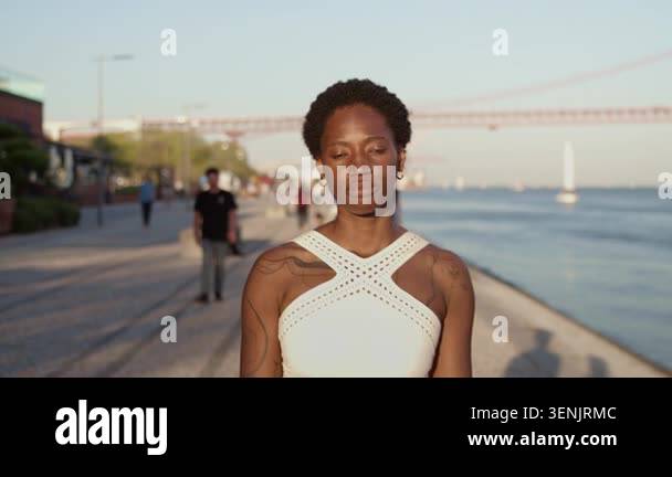 Black woman standing near waterfront promenade while camera slowly ...