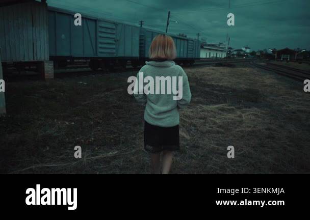 Rear view of a young woman standing near freight train cars beside ...