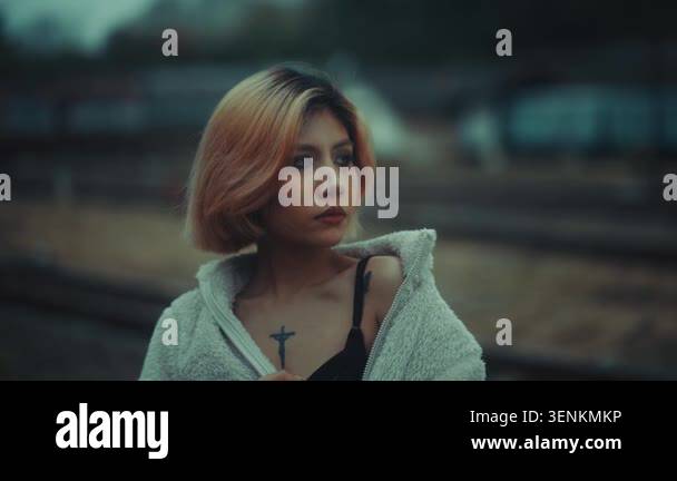 A young blonde woman stands near railway tracks at dusk, slightly ...