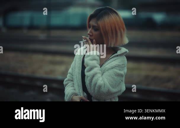 A young blonde woman stands near railway tracks at dusk, slightly ...