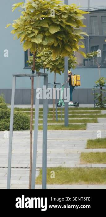 A delivery person rides an electric scooter through a modern urban ...