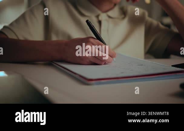 A concentrated teenage boy sits at his desk at night, writing notes in ...