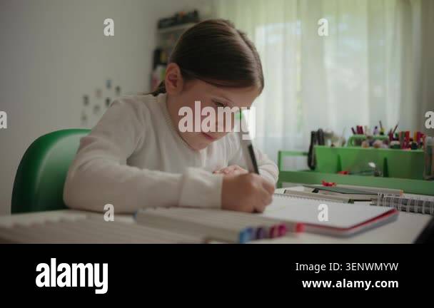A young girl sits at her desk in her room, focused on drawing in a ...