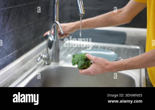 Close up of hands rinsing fresh broccoli beneath flowing tap water in ...