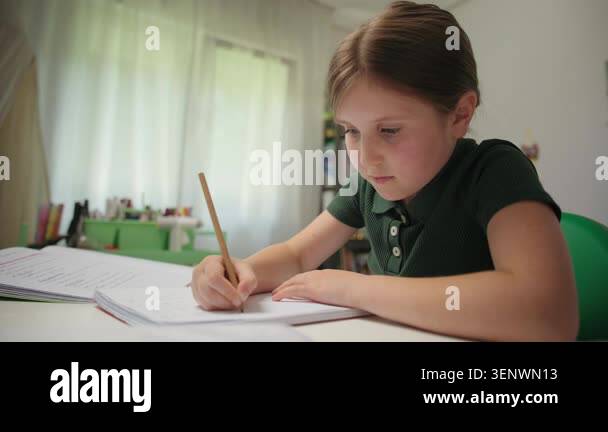 A focused young girl sits at her desk at home, diligently writing in a ...