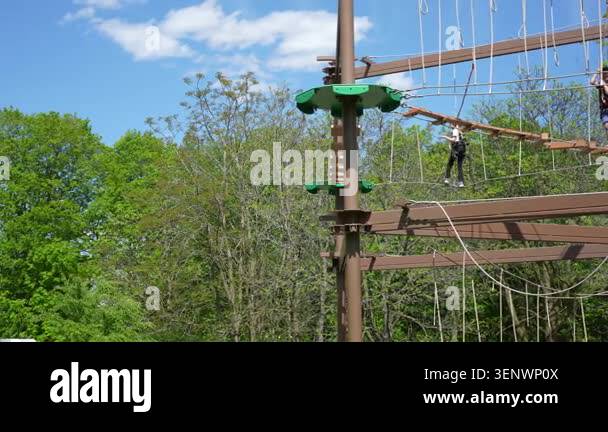 A person moves across an elevated rope bridge in a wooded adventure ...