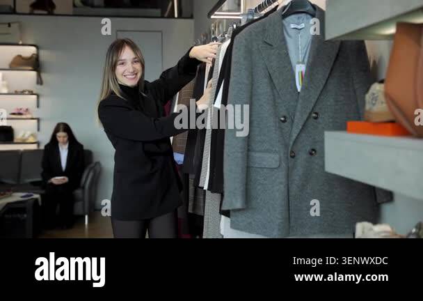 Woman shopping for clothes in a fashion boutique, smiling while looking ...