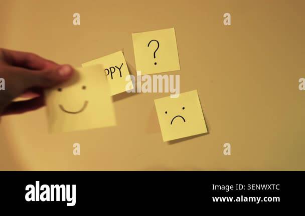 Human hand replacing a sticky note with a sad emoticon for one with a ...