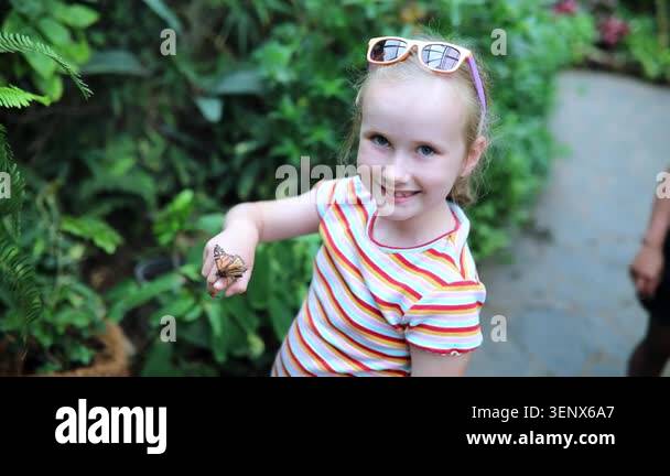Curious young girl watching a butterfly up close in a tropical ...