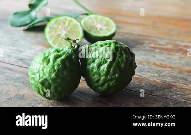 Fresh green kaffir limes with blurred sliced halves on wooden table ...