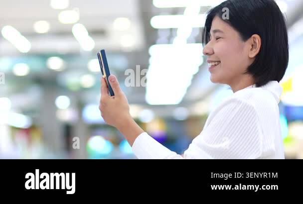Smiling Asian businesswoman using smartphone for video call in a modern ...