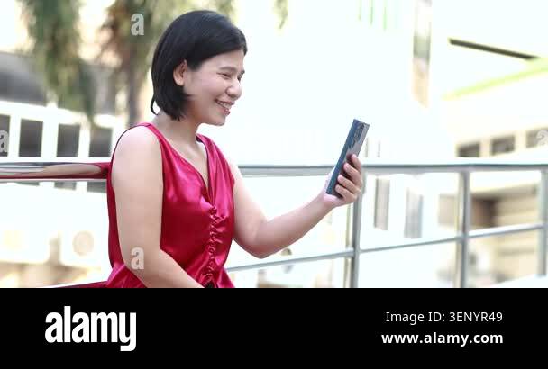 Smiling woman waving during a video call on a smartphone outdoors ...