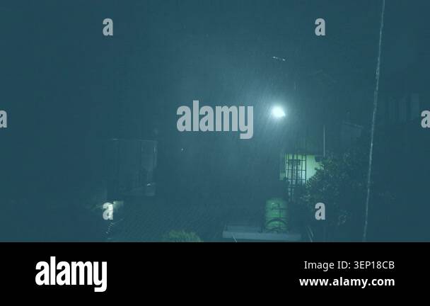 A solitary street lamp casts a glow on a dark, misty night, revealing ...