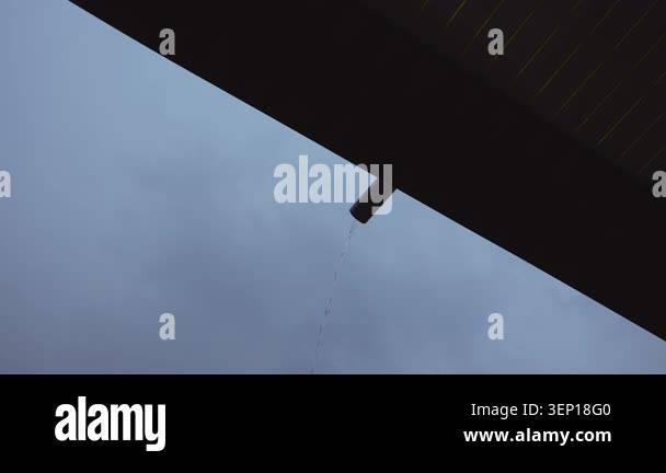 Water droplets fall from a building's gutter against a moody, overcast ...