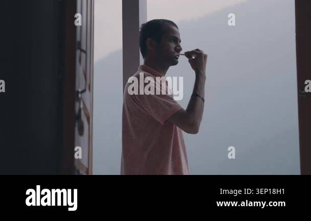 A man brushes his teeth in silhouette against a misty mountain backdrop ...
