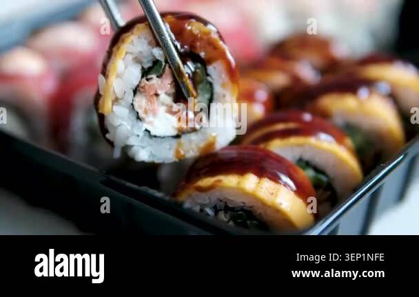 Metal chopsticks pick up a sushi roll filled with tender tuna, creamy ...