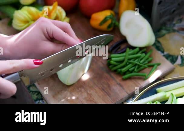 Fresh pattypan squash is being sliced on a wooden cutting board ...
