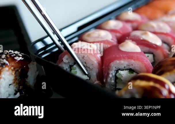 Metal chopsticks carefully lift a piece of tuna sushi topped with a ...
