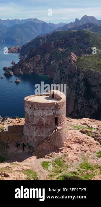 An ancient stone Genoese Tower overlooks a stunning bay with clear blue ...