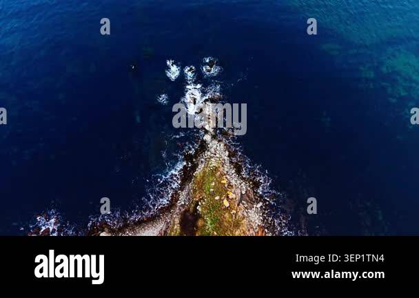 Overhead drone perspective of a narrow stone peninsula surrounded by ...
