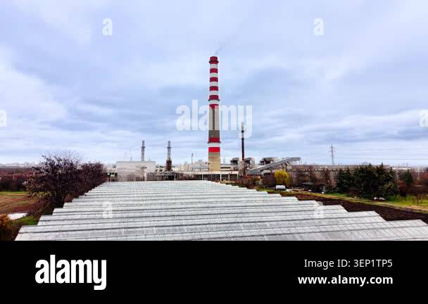 Industrial chimney with red and white stripes above greenhouses ...