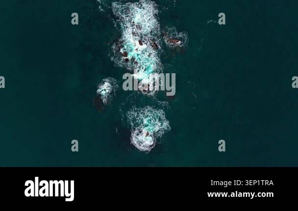 Aerial view of white surf swirling around submerged dark stones in dark ...