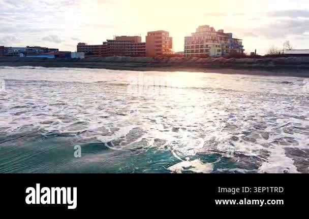 Low-angle view looking over choppy green sea waves toward seaside ...