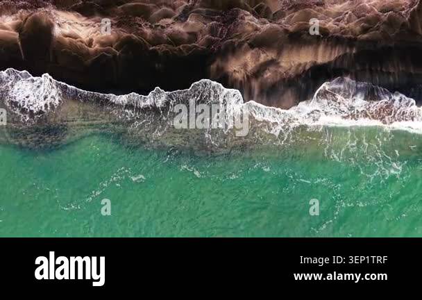 Direct overhead view of white surf meeting dark volcanic shoreline and ...