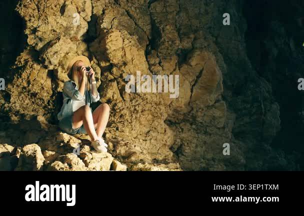 woman in a hat sits in a rocky cave and looks at the camera Stock Video ...