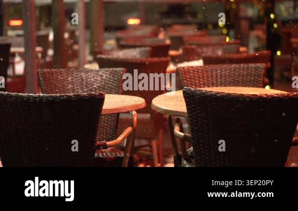 Empty tables and chairs of outdoor cafe on snowy street in evening ...
