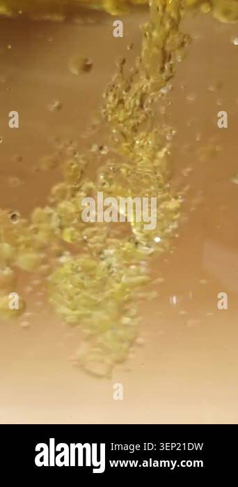 Close-up macro view of golden cosmetic oil bubbles floating and merging ...