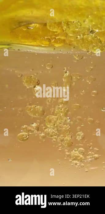 Close-up macro view of golden cosmetic oil bubbles floating and merging ...