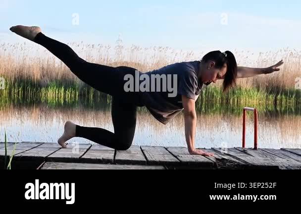 Athletic woman holds bird dog pose for core strength on wooden pier ...