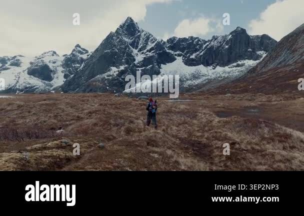 A solitary backpacker stands in the foreground of a vast alpine valley ...